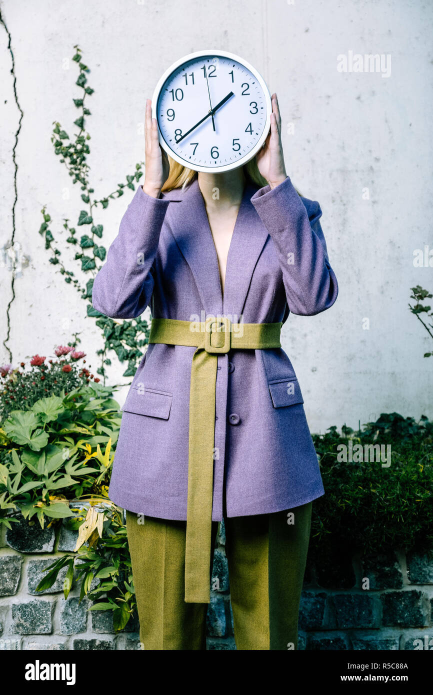 Clock near face. Photo model wearing stylish purple jacket and green ...