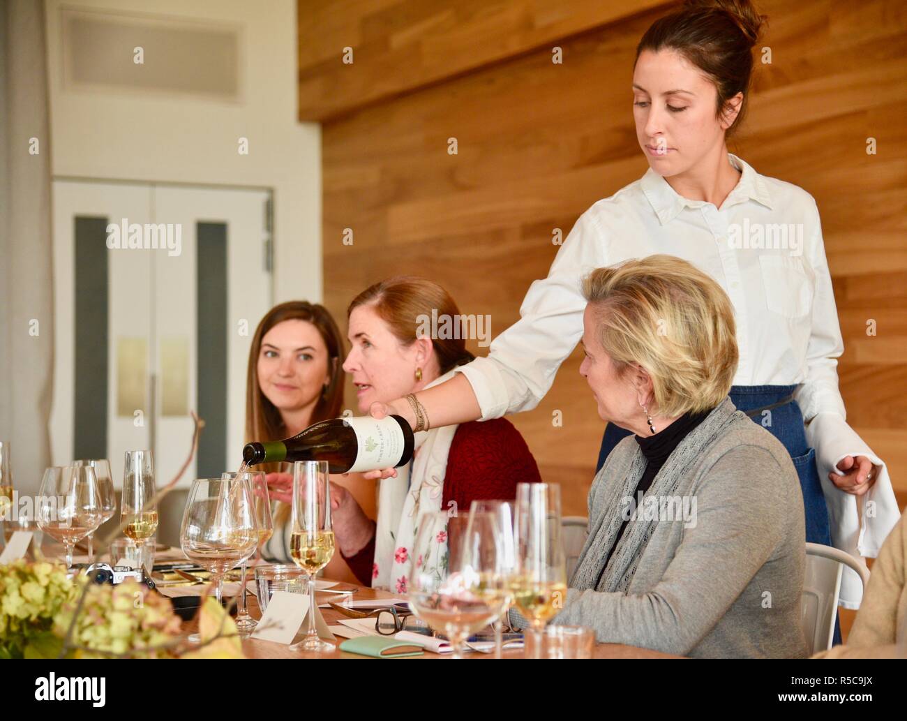 Attractive woman waitress pouring wine from a bottle into glasses at a ...