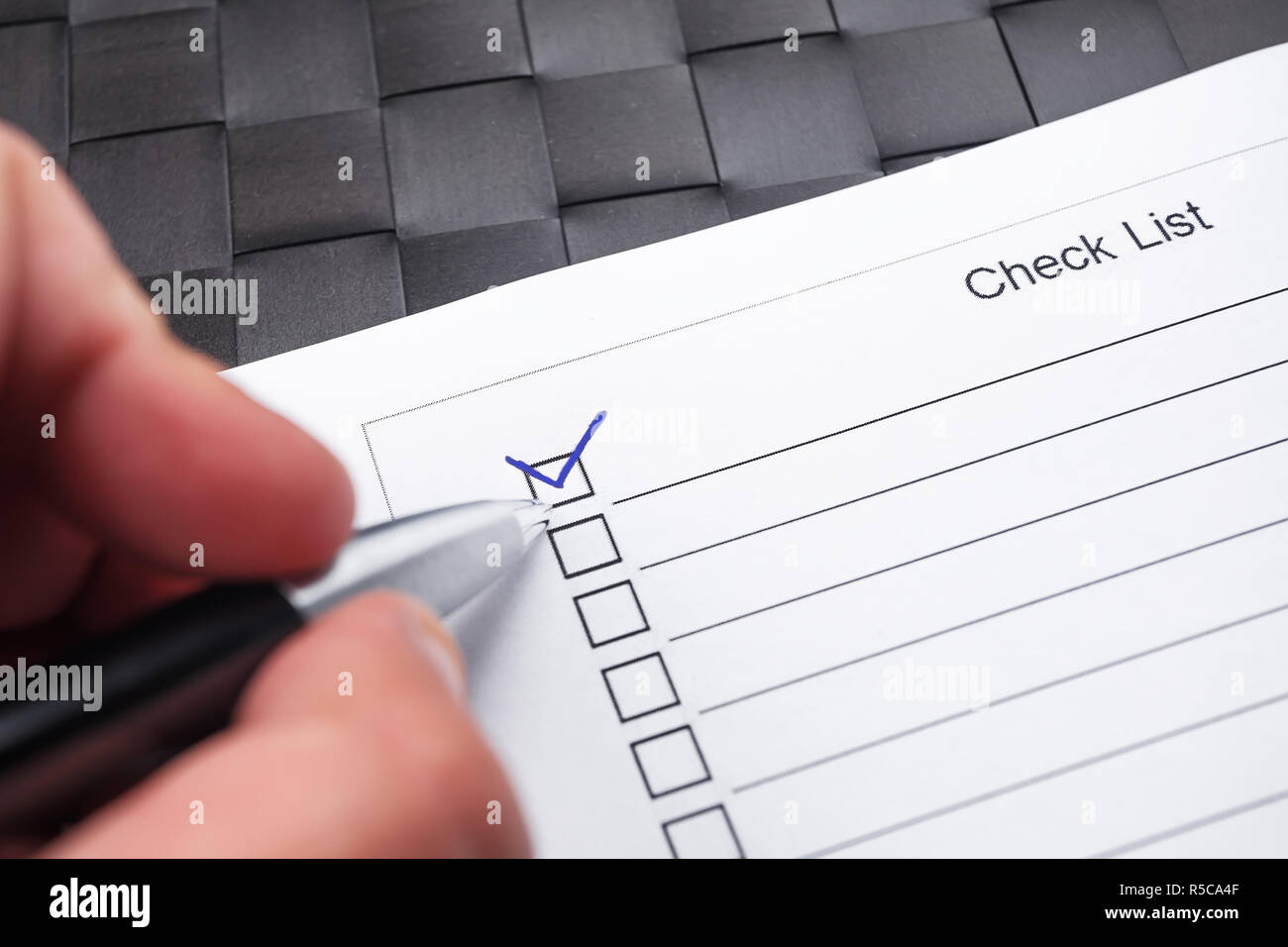 Checklist with hand doing tick mark with a pen on checkered black ...