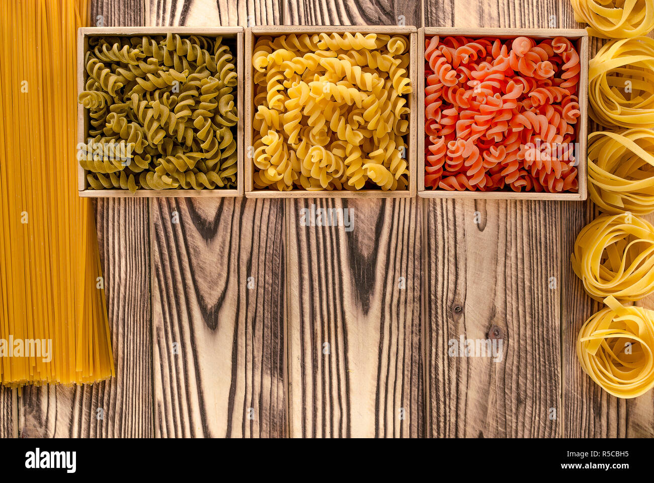 Three wooden boxes with colored fusilli are on a wooden background next ...