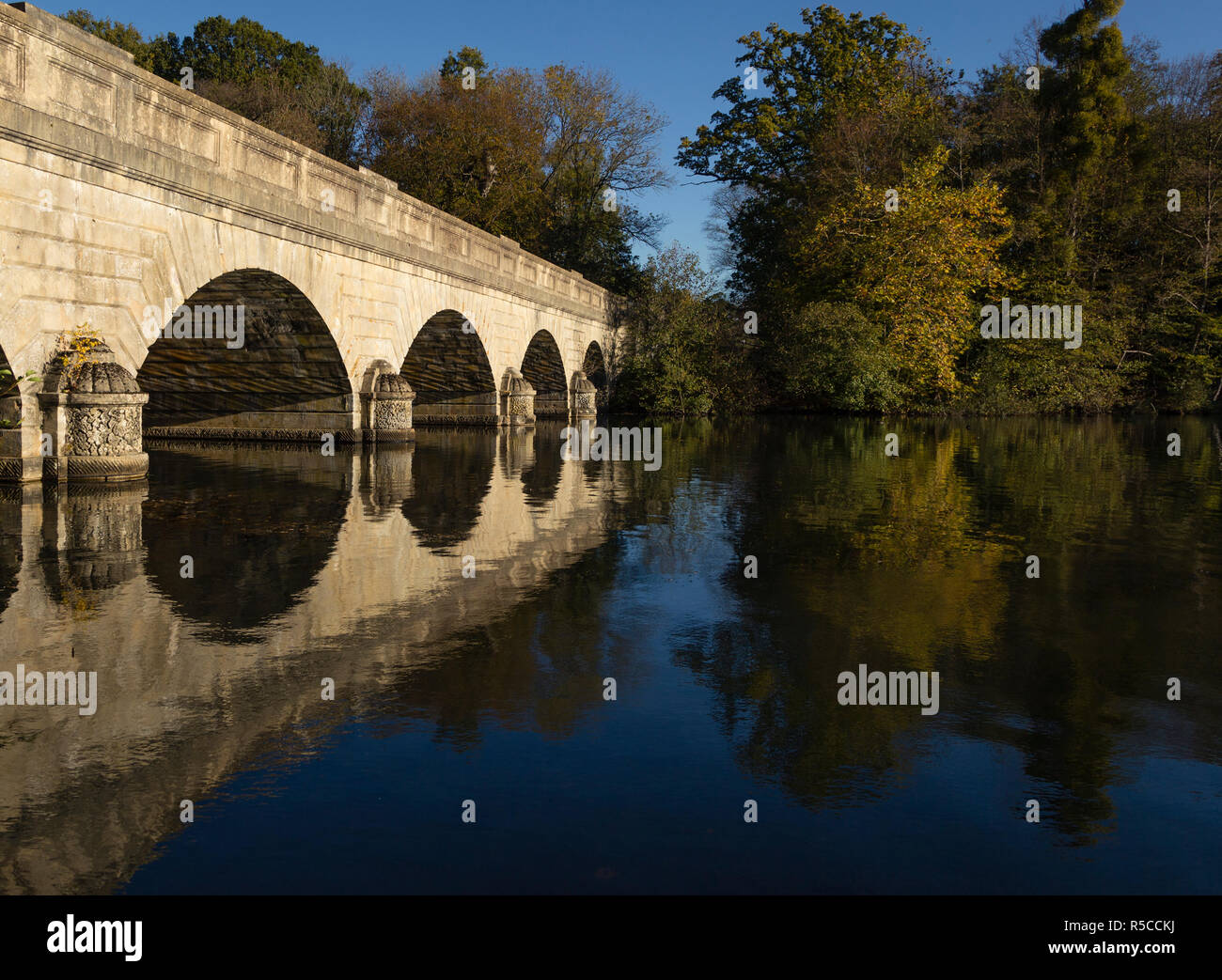 Arched bridge over still water, reflections in autumn Virginia Water ...