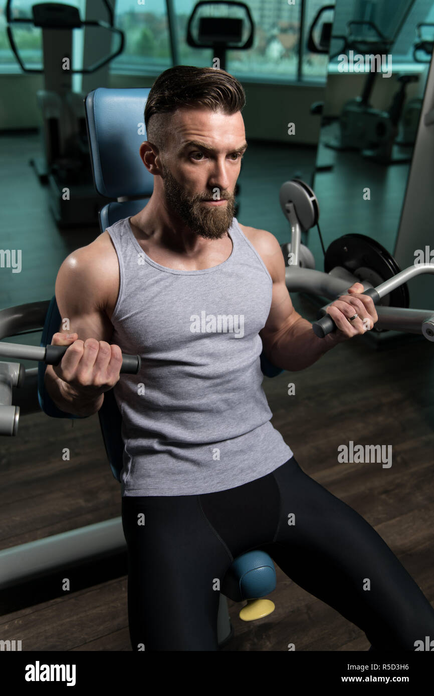 Man In The Gym Exercising On His Biceps On Machine With Cable In The ...