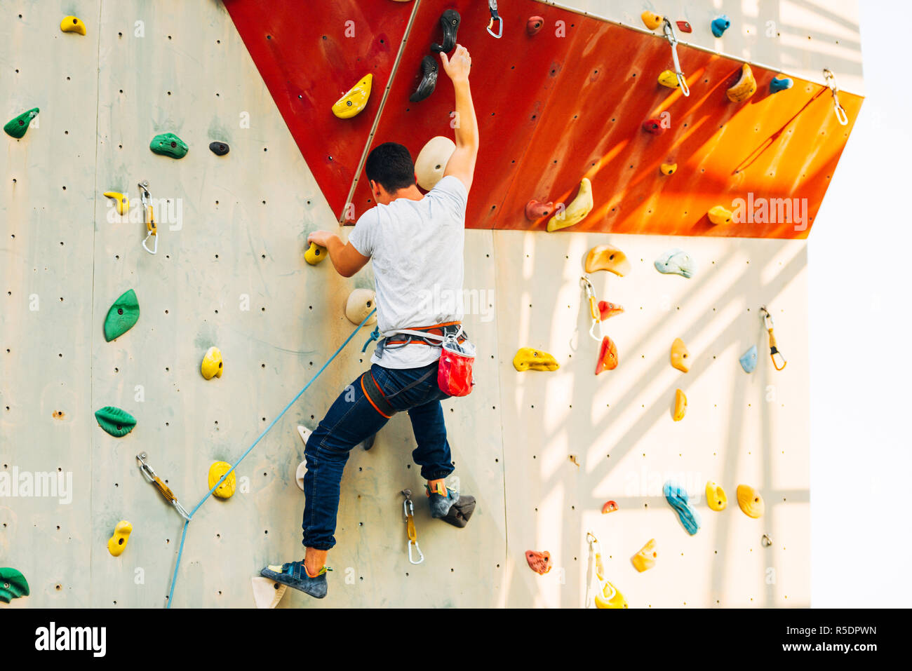 Man wearing belaying rope, climbing on a very high rock climbing wall ...