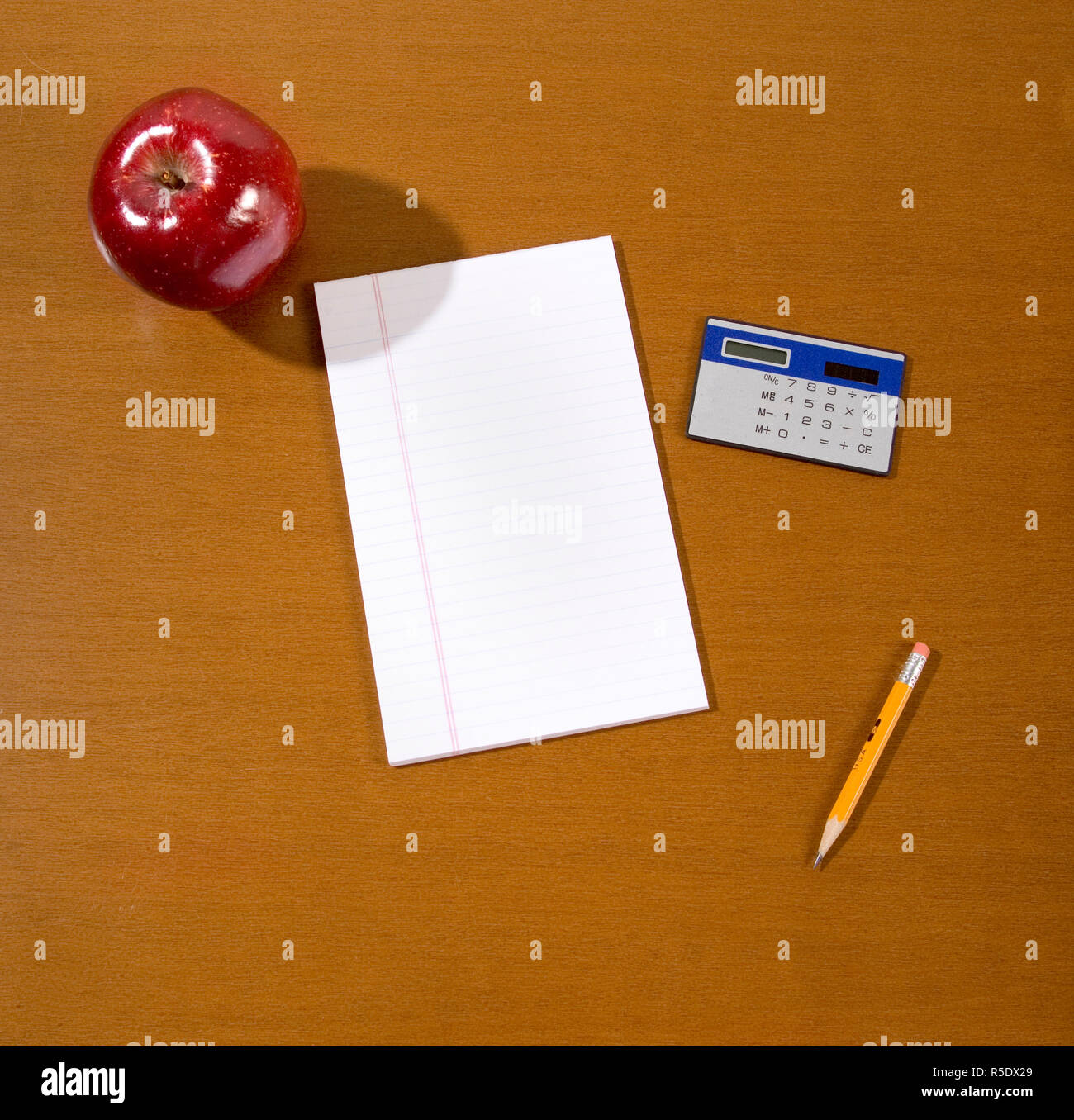 Teachers desk with short pencil, calculator, red apple, pad of paper ...