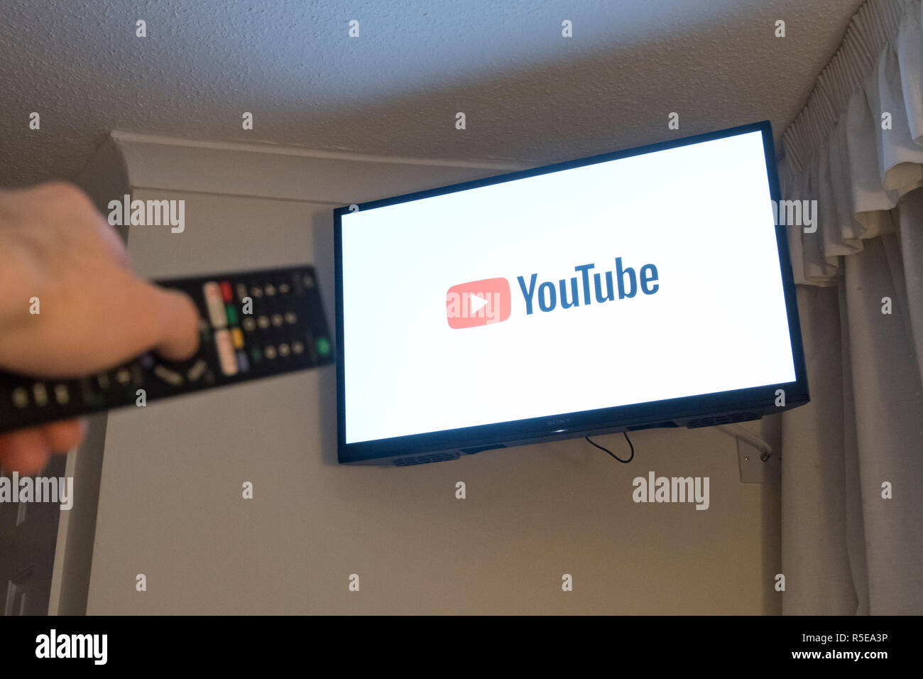 A man points a remote control at a smart television displaying the ...