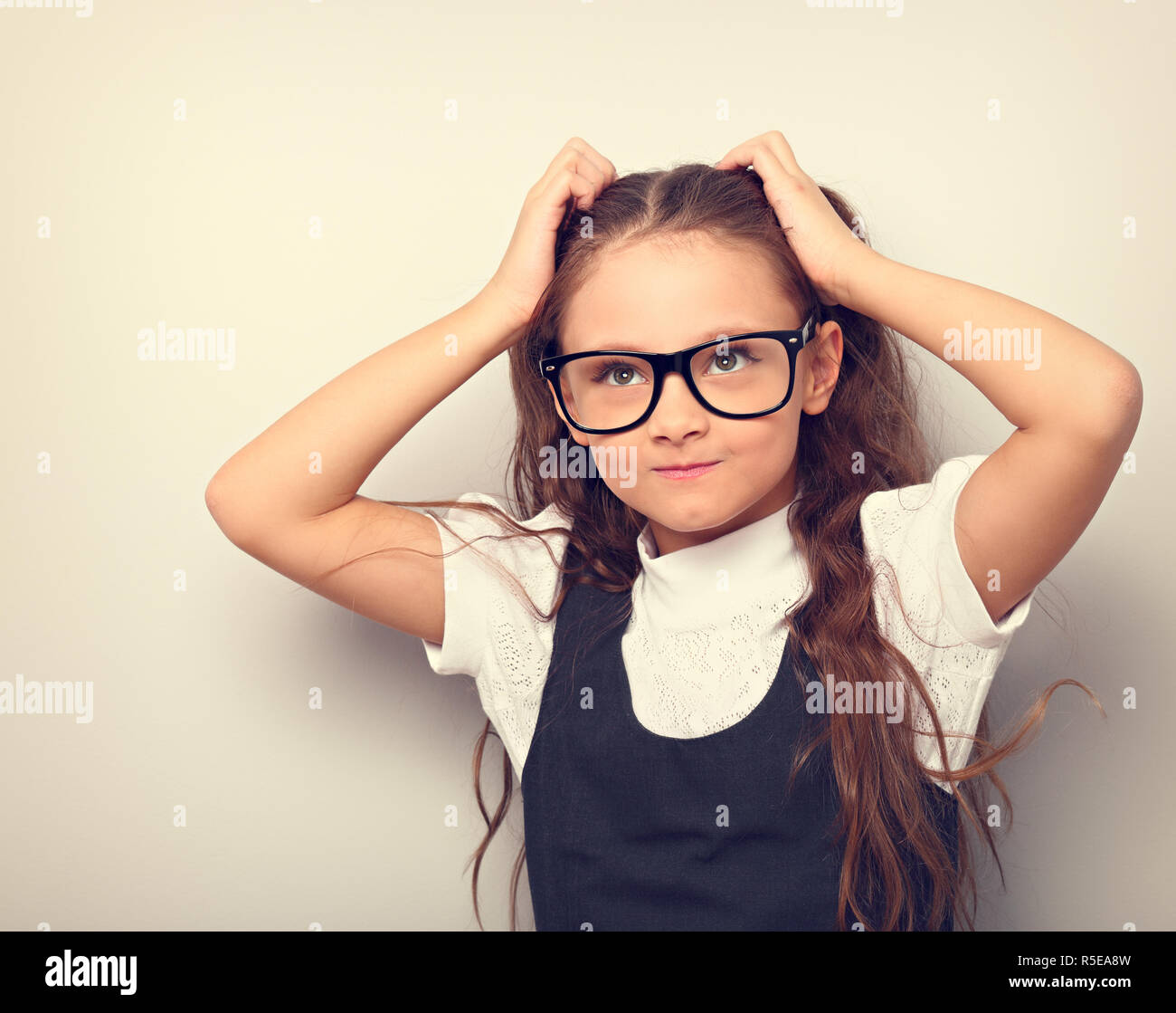 Fun happy pupil kid girl in eyeglasses scratching the head two hands ...