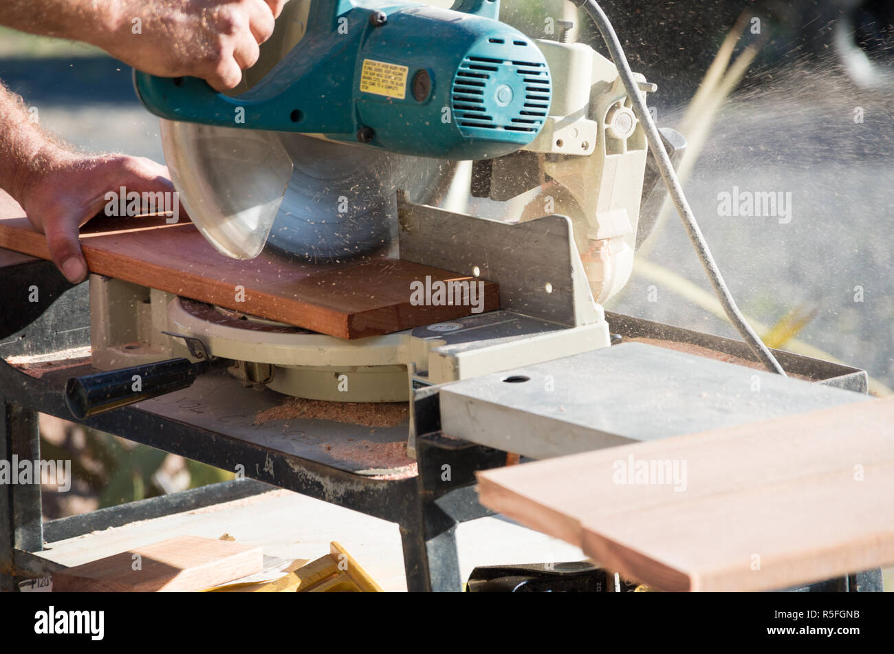 Man cutting wood with a saw outside in the sun during home renovations ...
