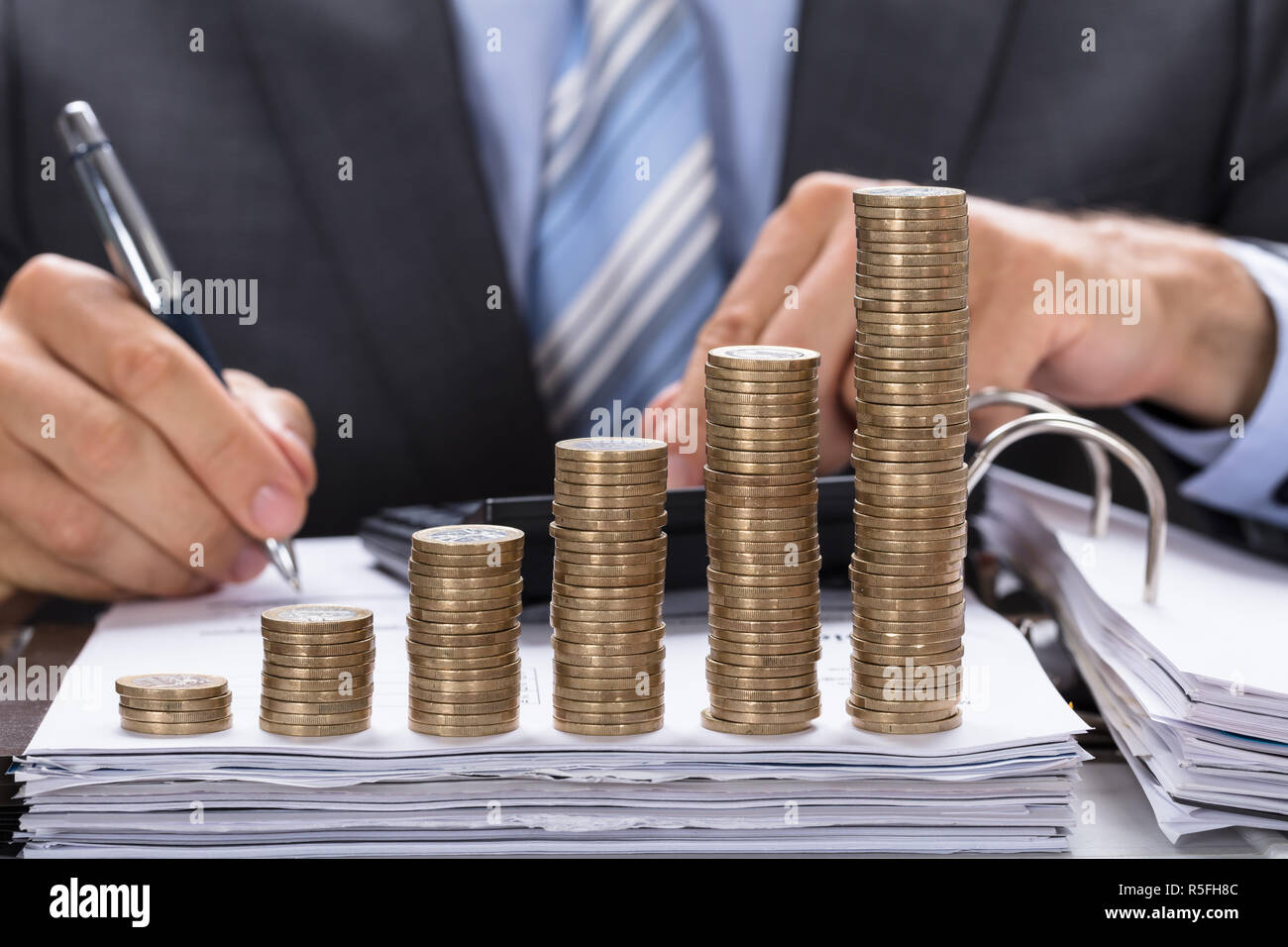 Businessman Calculating Invoice With Stacked Coins Stock Photo - Alamy