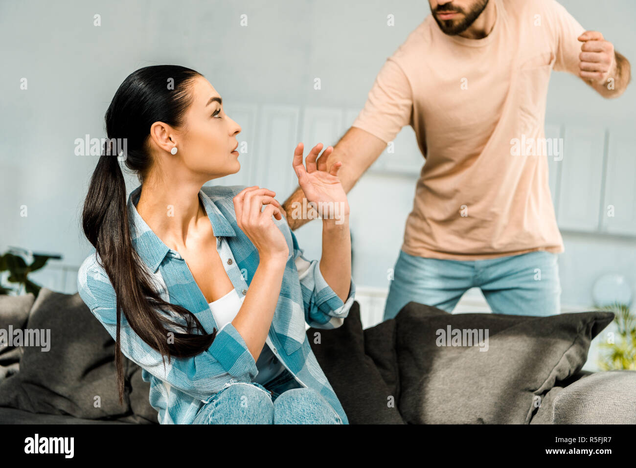 agressive husband trying to hit scared wife sitting on couch at home ...