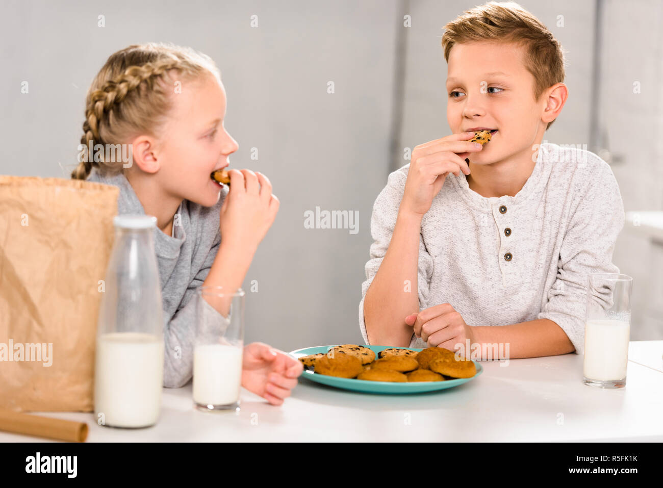 happy children eating cookies and drinking milk at table in kitchen ...