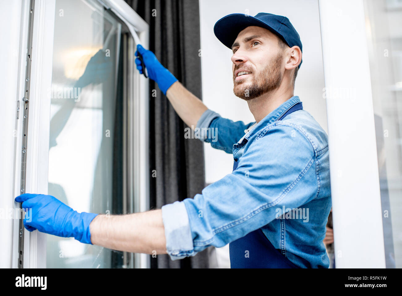 Man as a professional cleaner in blue uniform washing window with ...