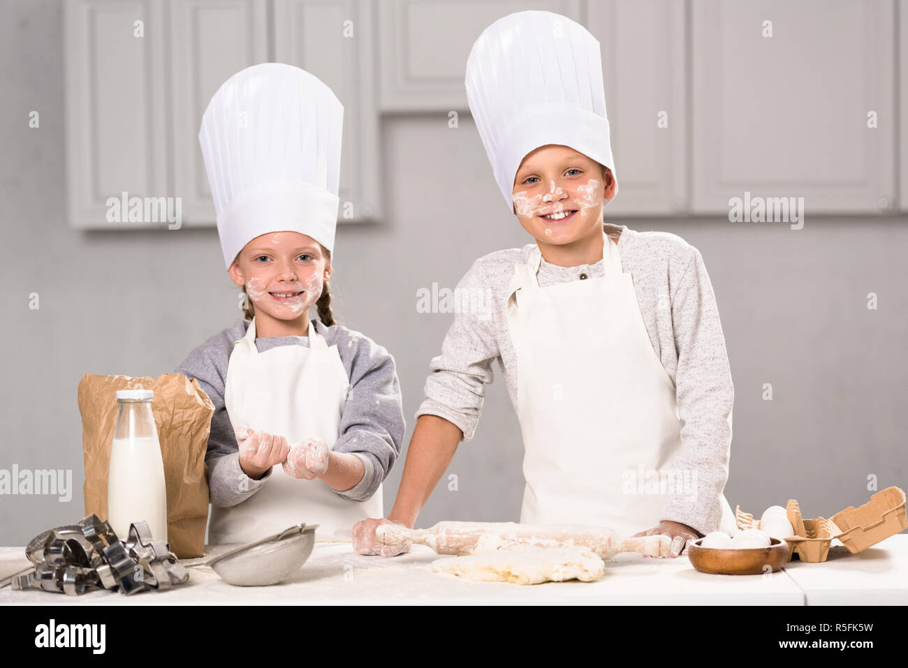 sister and brother in chef hats having fun with flour at table in ...