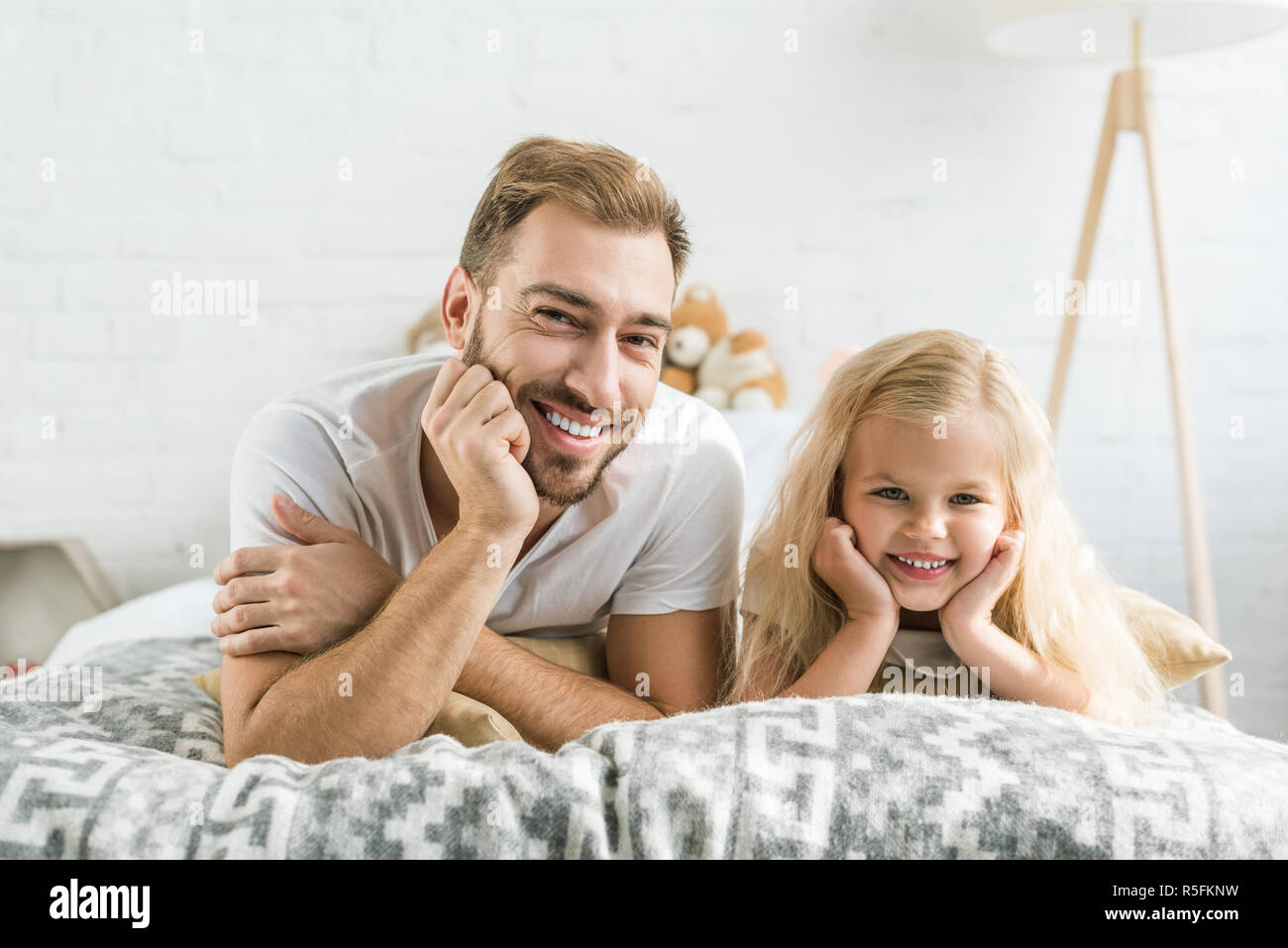happy father and cute little daughter lying together on bed and smiling at camera Stock Photo ...