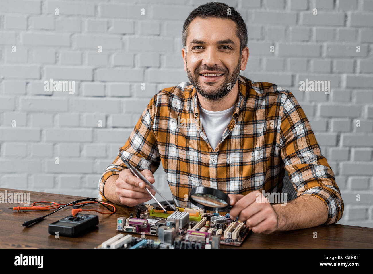 handsome smiling computer engineer with tweezers and magnifying glass ...