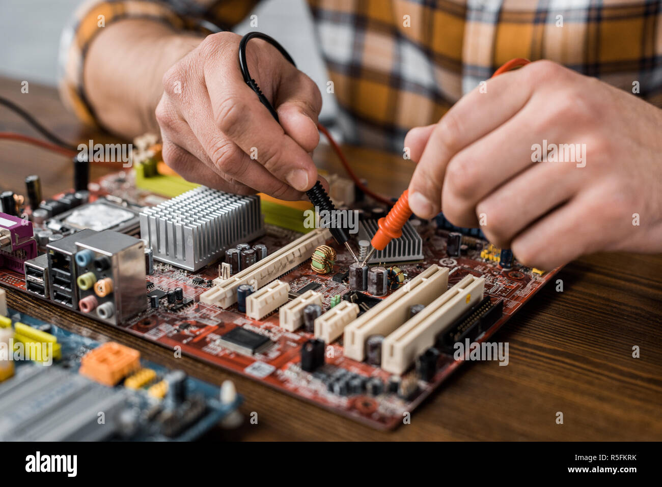cropped shot of computer engineer with tester examining motherboard ...