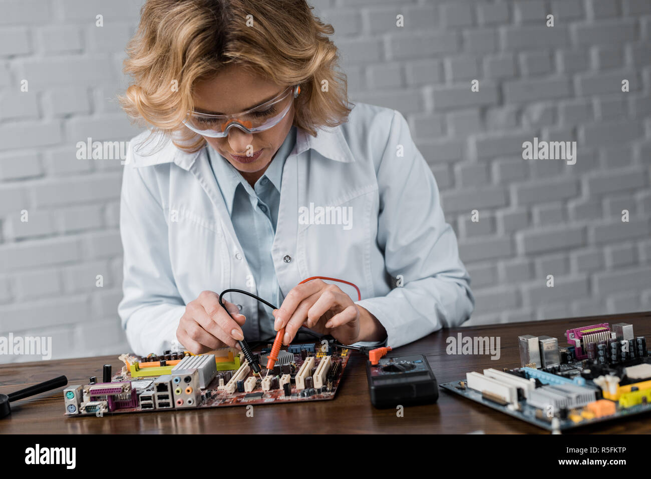 concentrated female computer engineer with tester examining motherboard ...