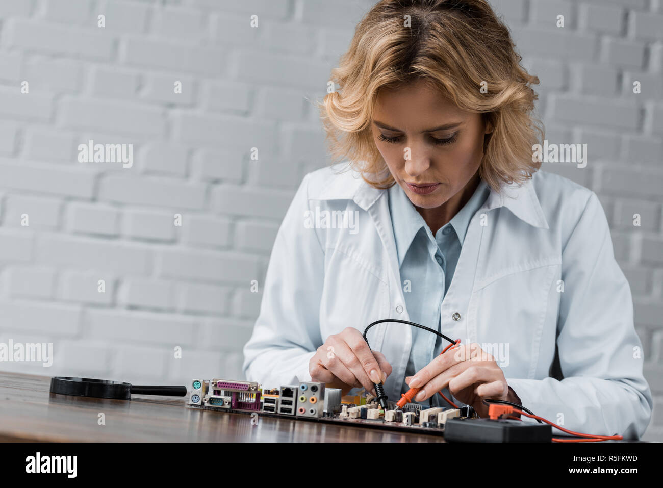 female electronic engineer with tester examining computer motherboard ...