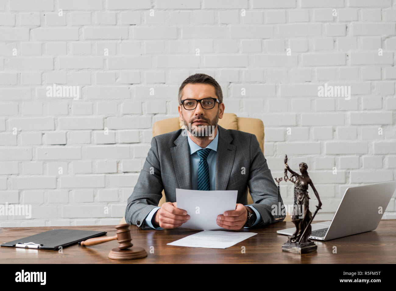 serious judge in eyeglasses working with papers and looking at camera ...