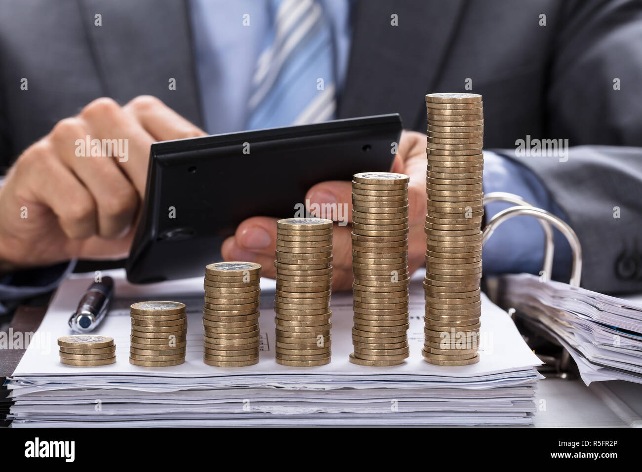 Businessman Calculating Invoice With Stacked Coins Stock Photo - Alamy