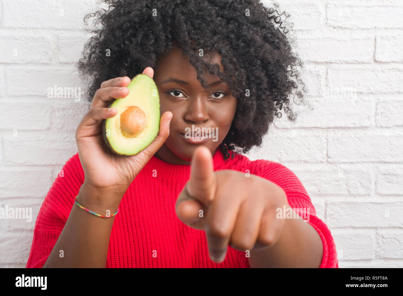 Young african american woman over white brick wall eating avocado ...