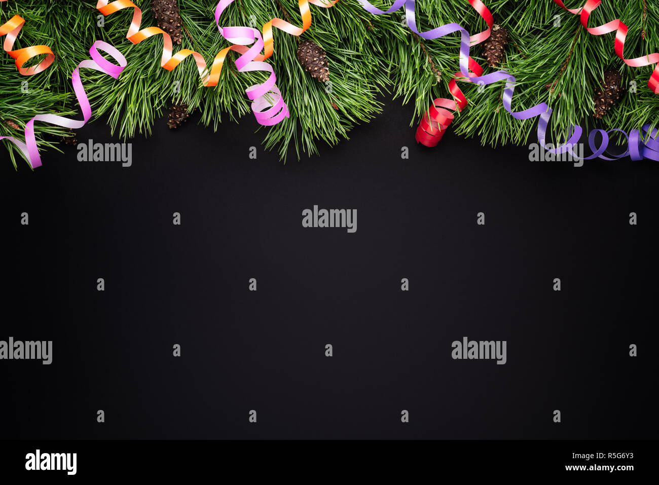 Christmas border with fir branches and festive streamers on a black ...