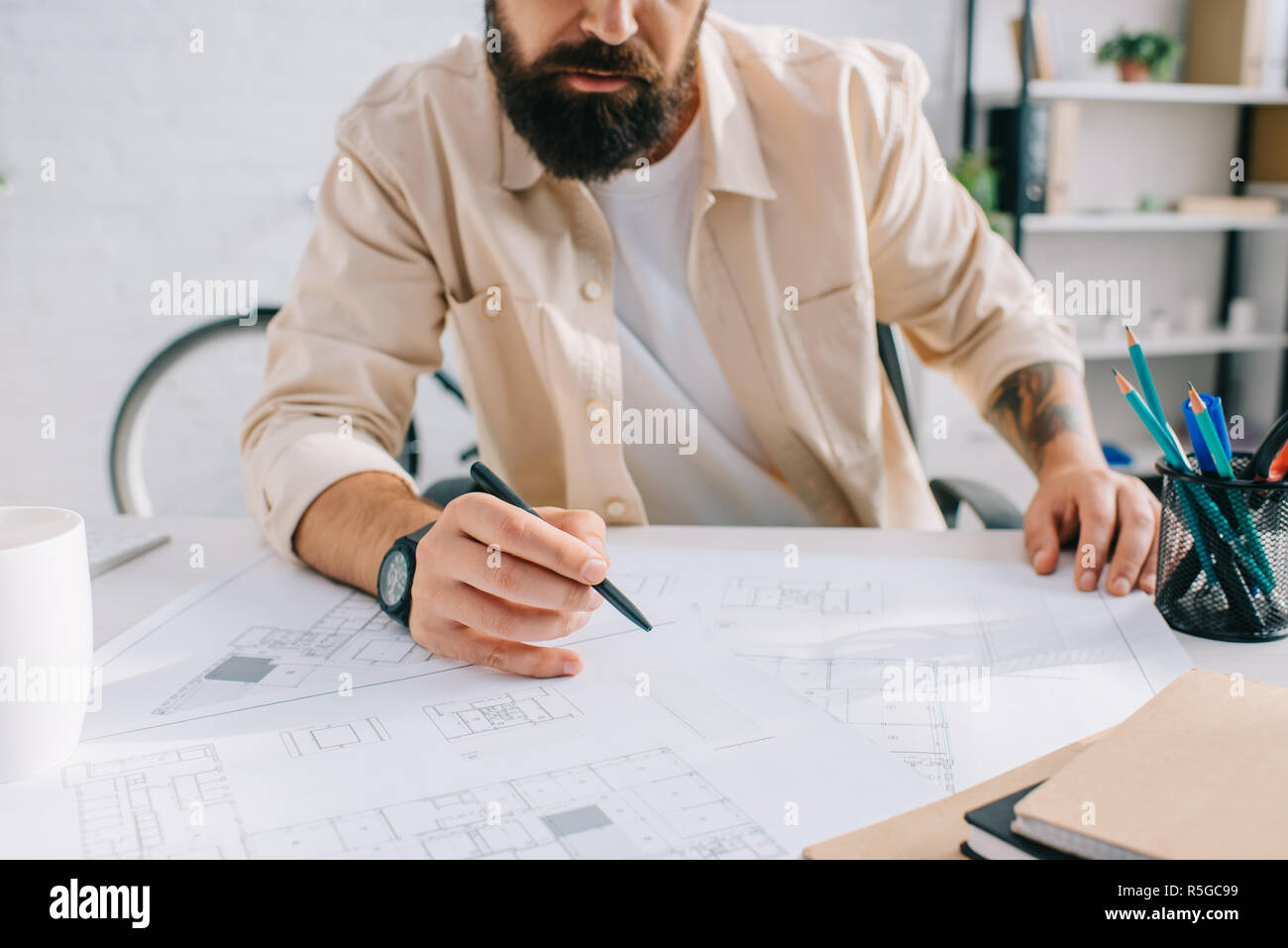 Bearded architect sitting at desk and working with blueprints Stock ...