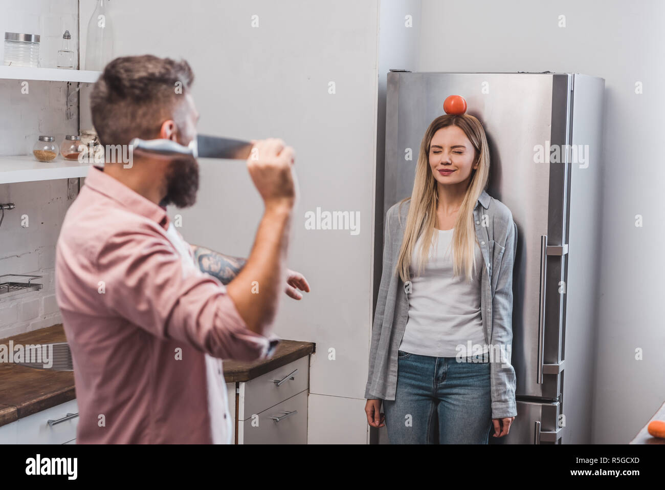 man throwing sharp knife at tomato on woman head Stock Photo - Alamy