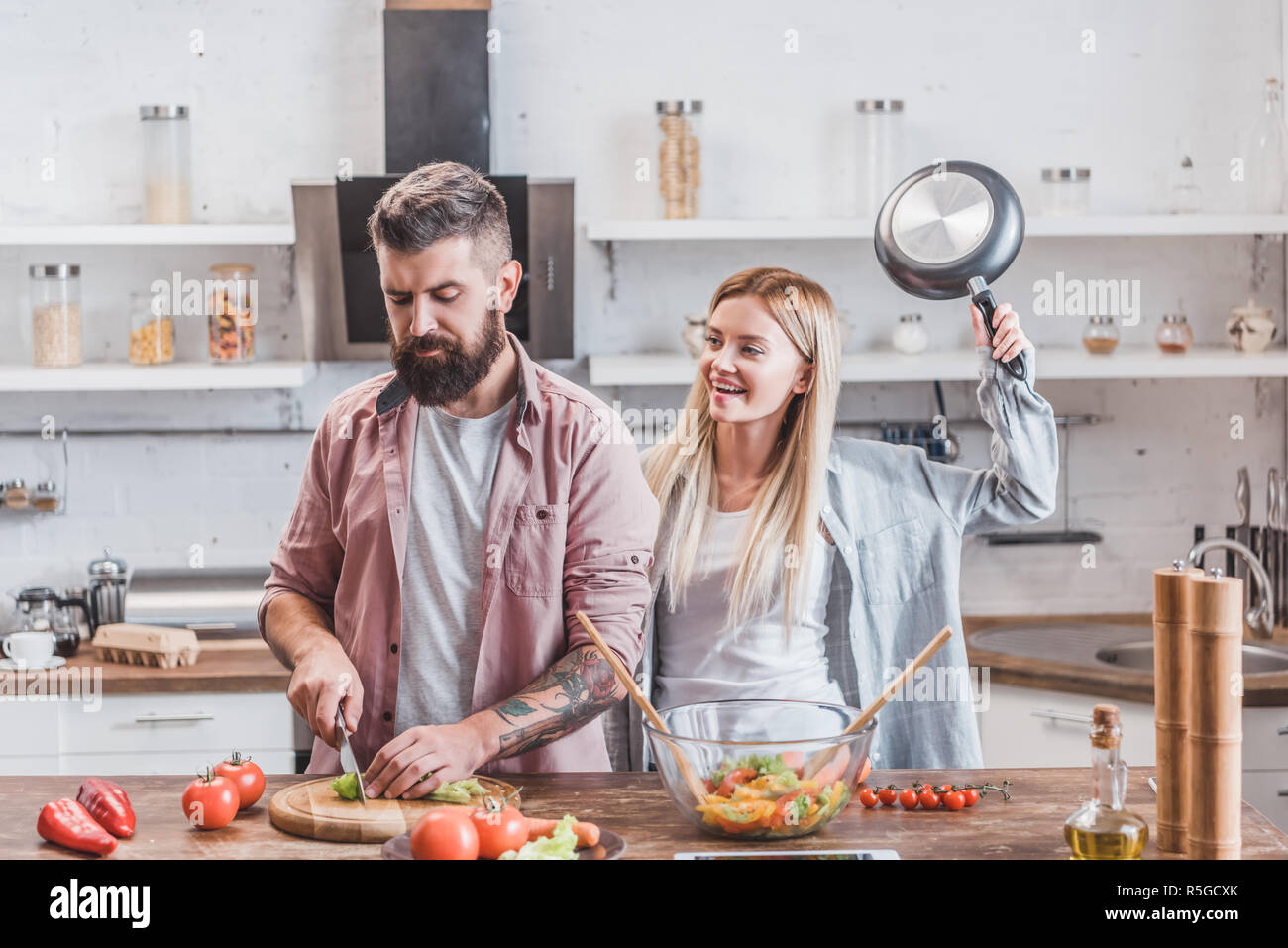funny girl joking and raising metal pan for hitting man at kitchen ...