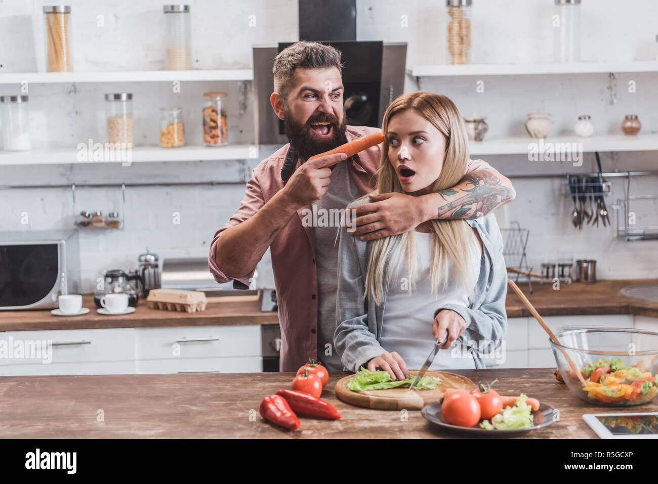 funny man putting carrot near woman head while scared girl cooking ...