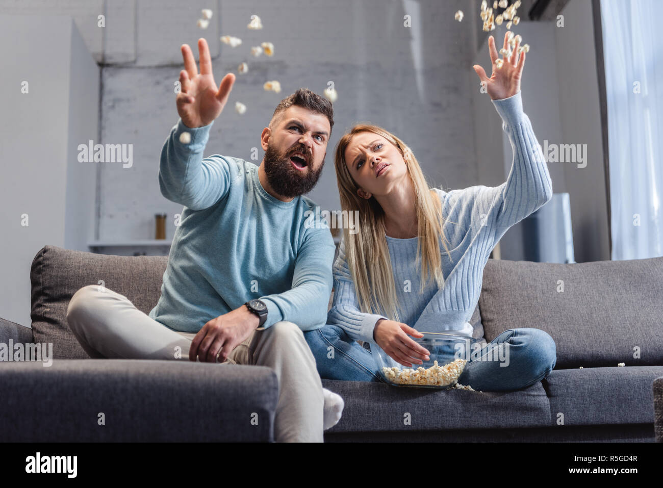 Emotional couple throwing popcorn and sitting on sofa Stock Photo - Alamy