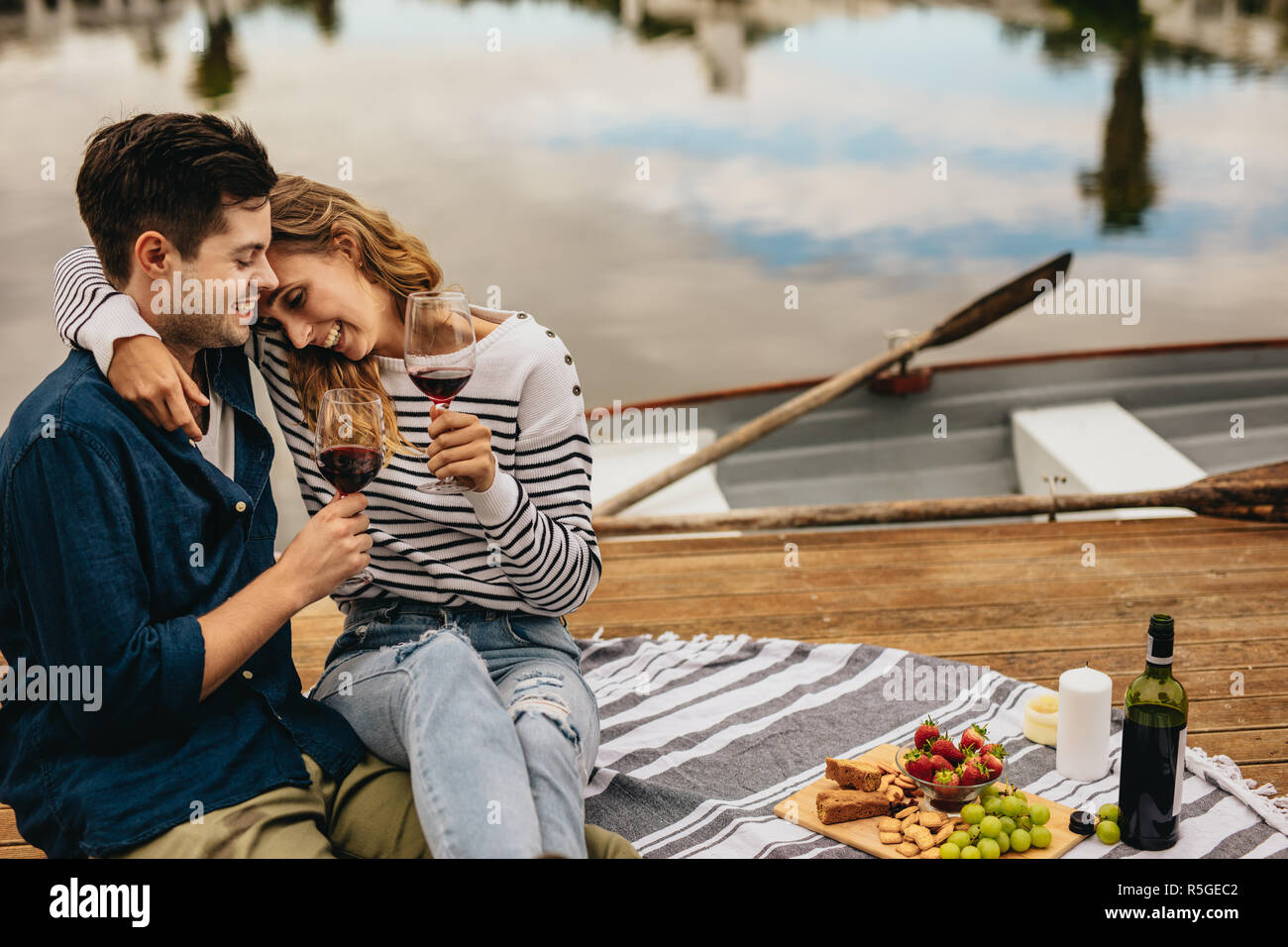 Romantic couple on a date sitting beside a lake with snacks and wine ...