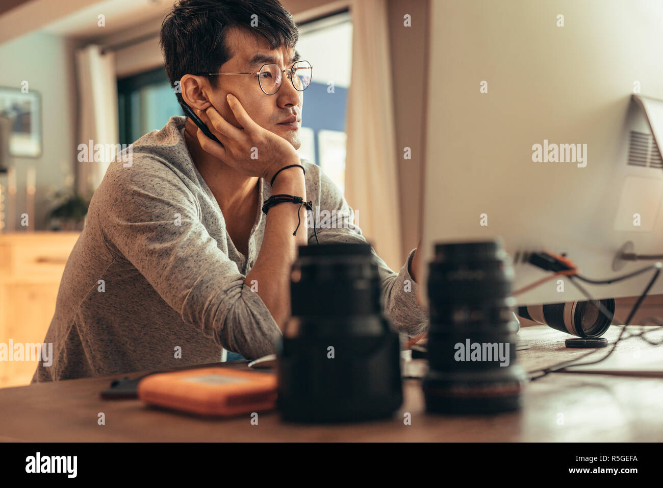 Male photographer looking at computer monitor and thinking while ...