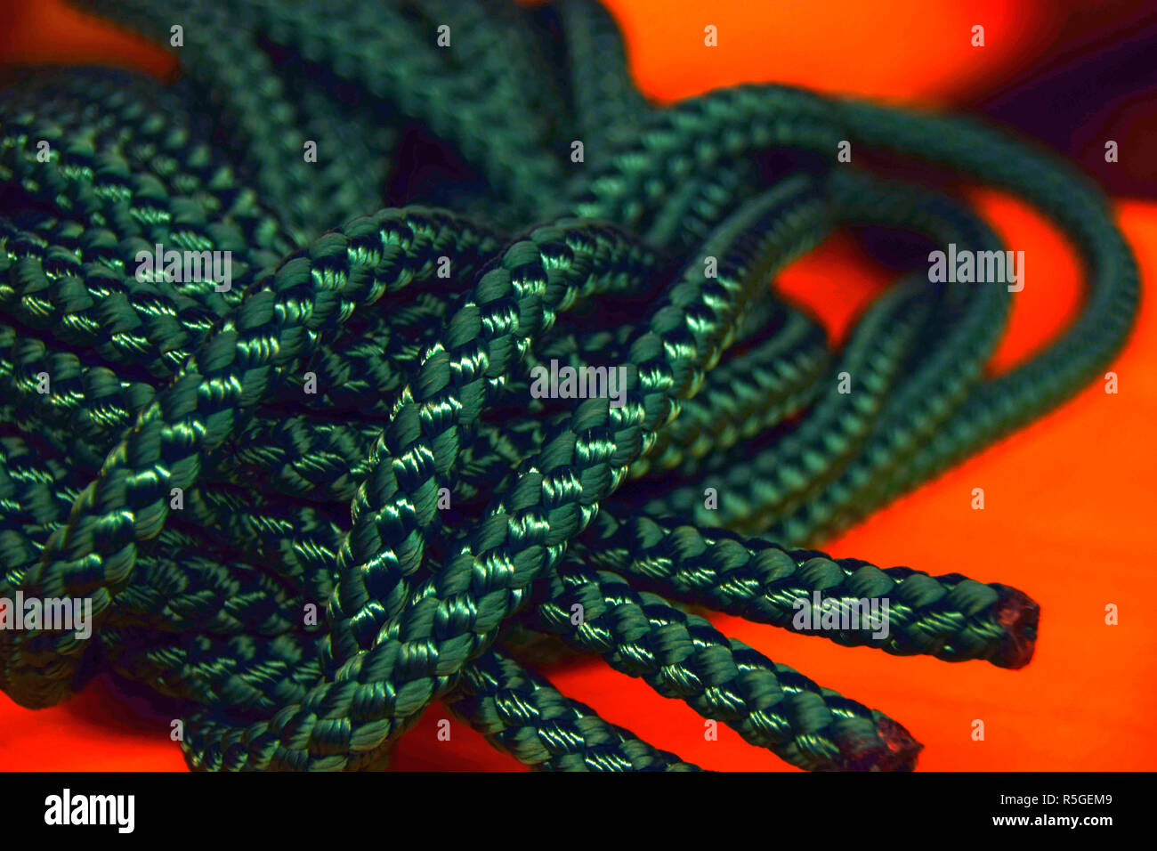 green nylon rope with focus to the ends in front of orange background ...
