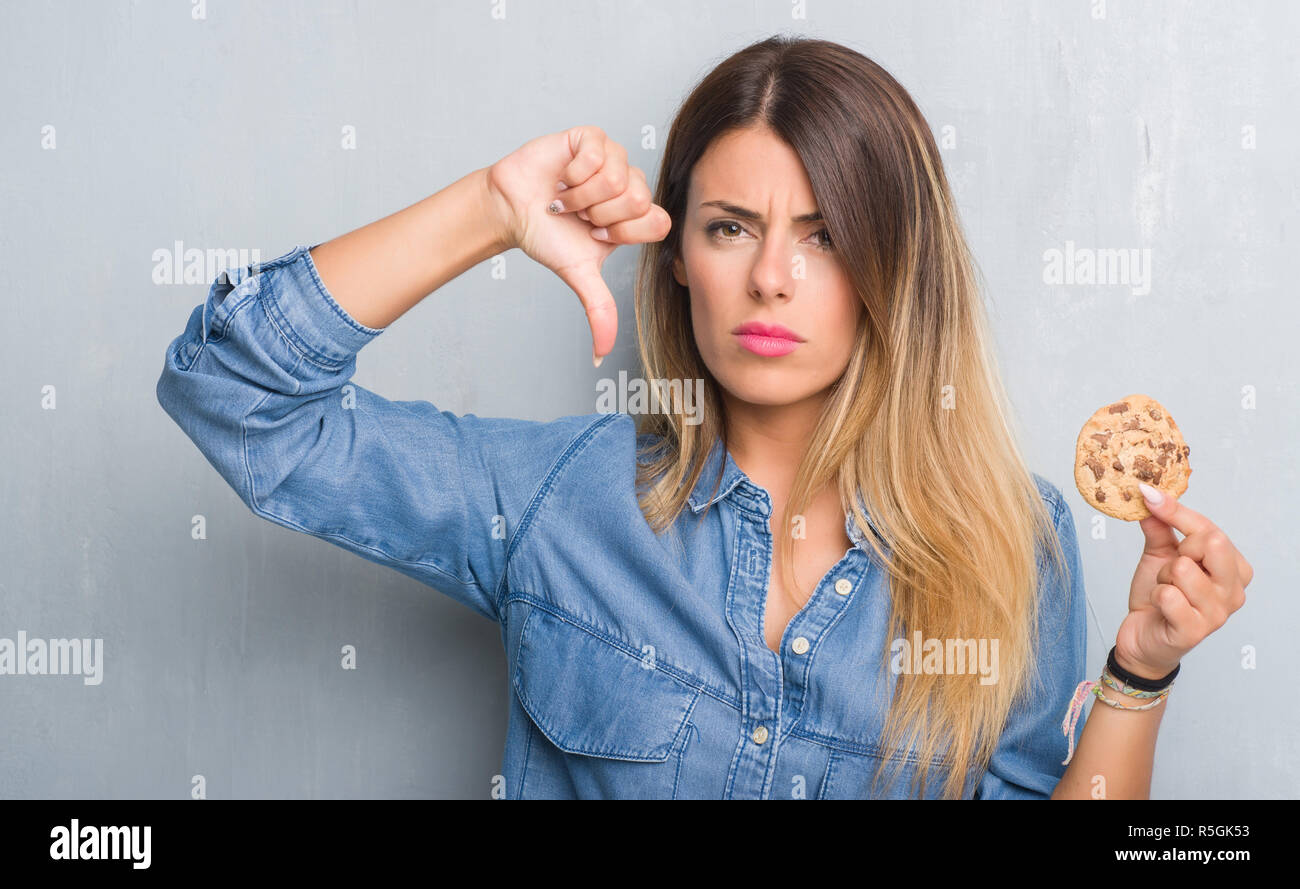 Young adult woman over grey grunge wall eating chocolate chip cooky ...