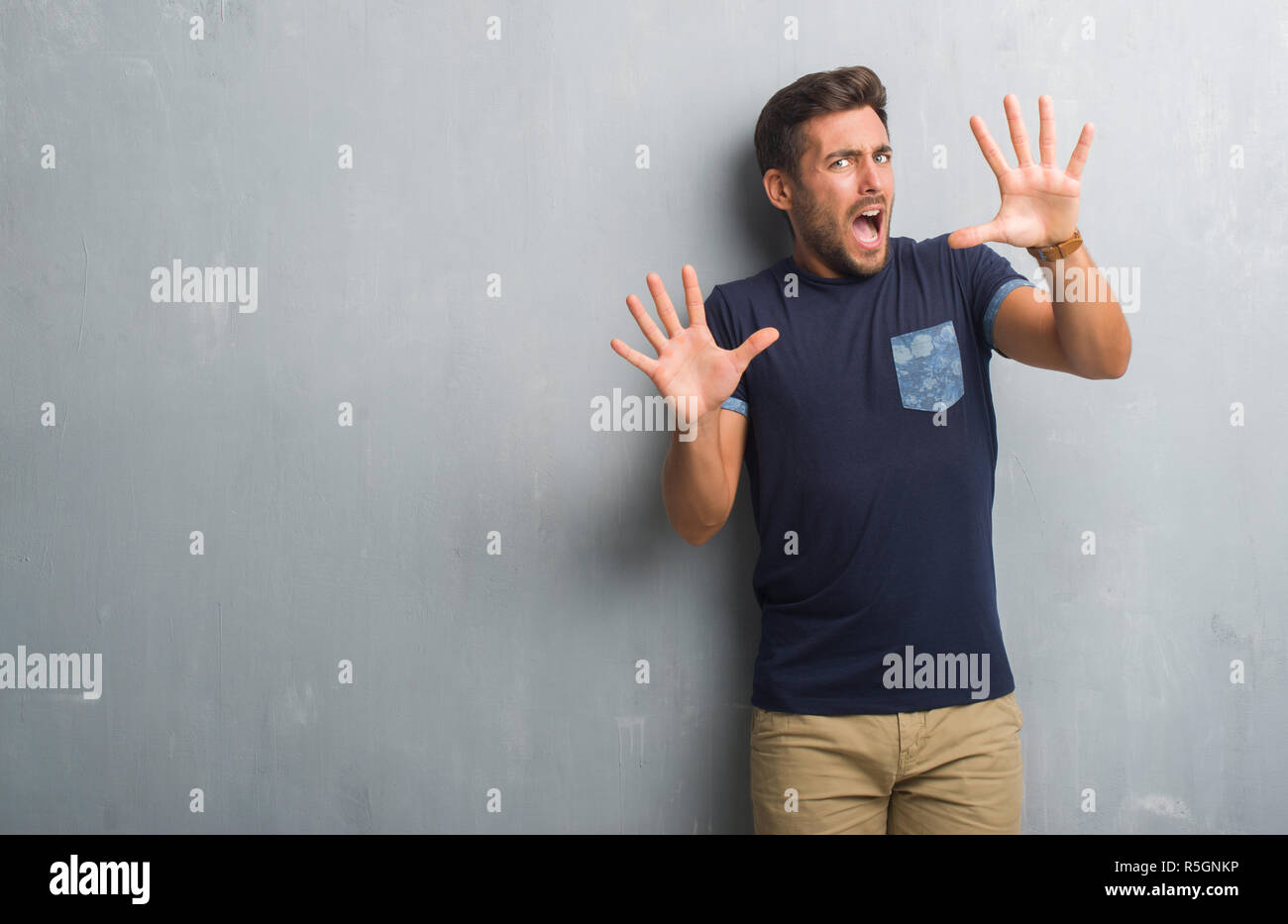 Handsome young man over grey grunge wall afraid and terrified with fear ...