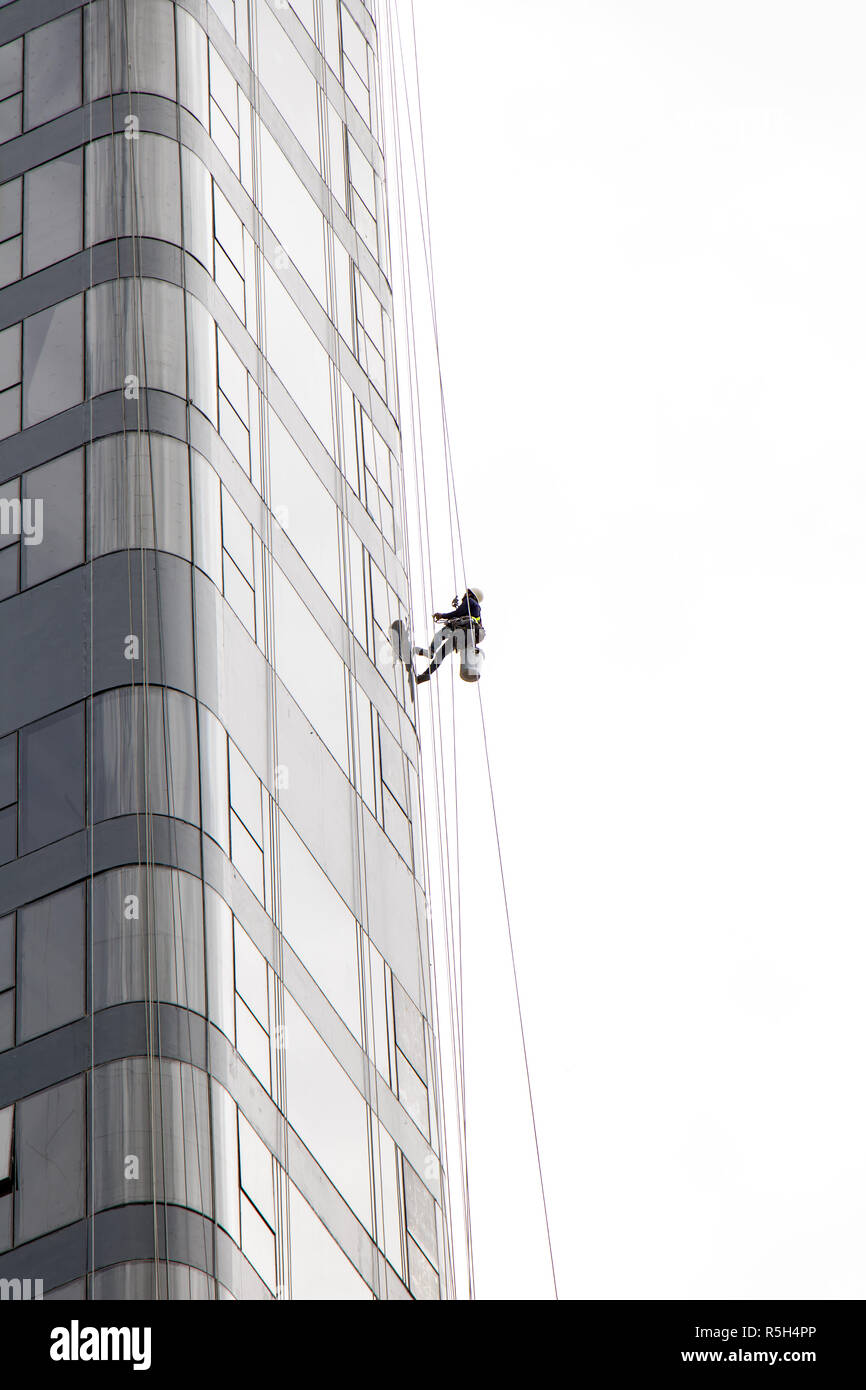 Man washes glass on high-rise building. Service cleaning the windows on ...