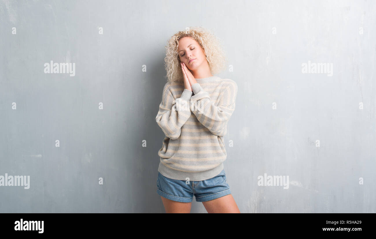Young blonde woman with curly hair over grunge grey background sleeping ...