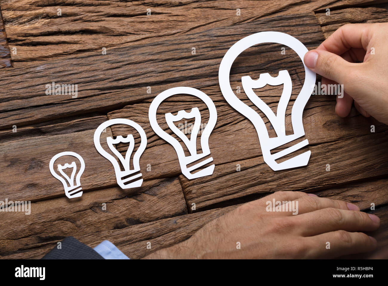 Businessman Arranging Paper Light Bulbs In Increasing Order Stock Photo ...