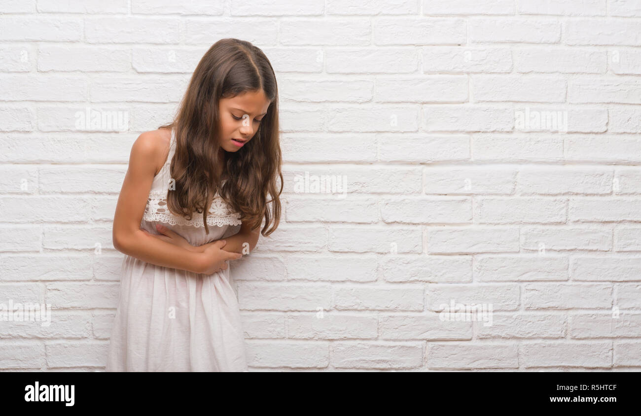 Young hispanic kid over white brick wall with hand on stomach because ...