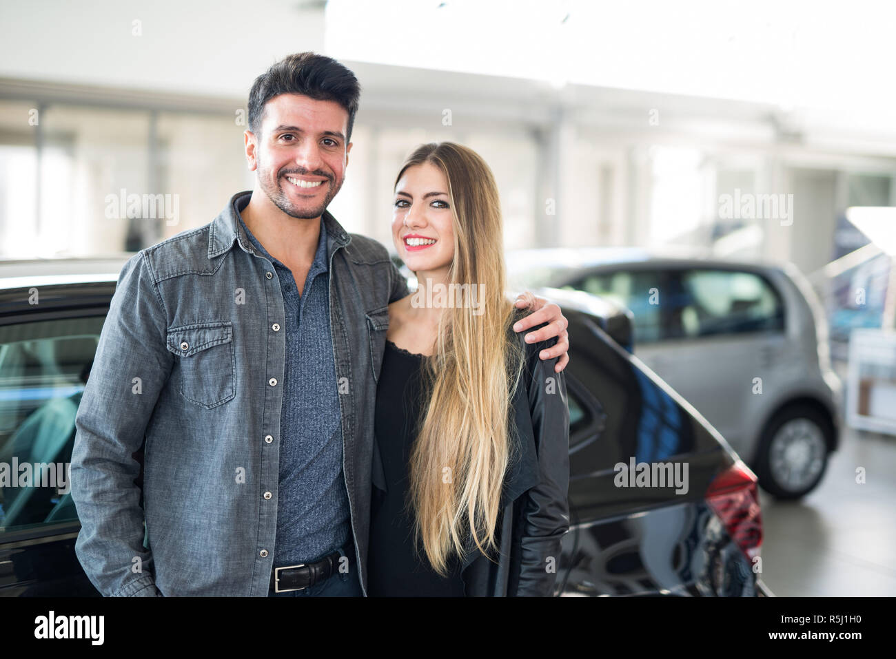 Happy couple in front of their new car in a showroom Stock Photo - Alamy