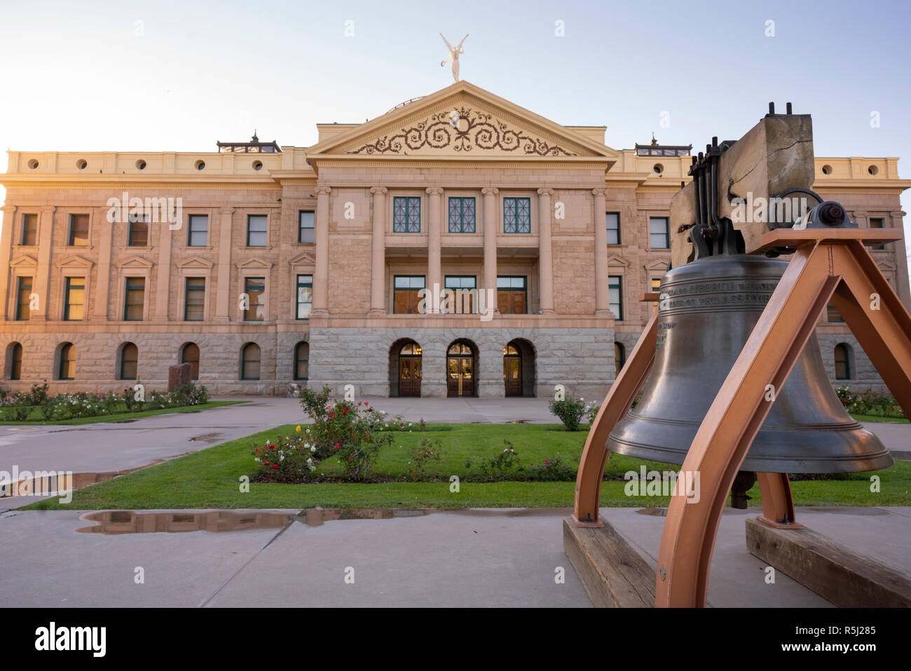 An old watchtower bell is mounted on the sidewalk in front of the state ...