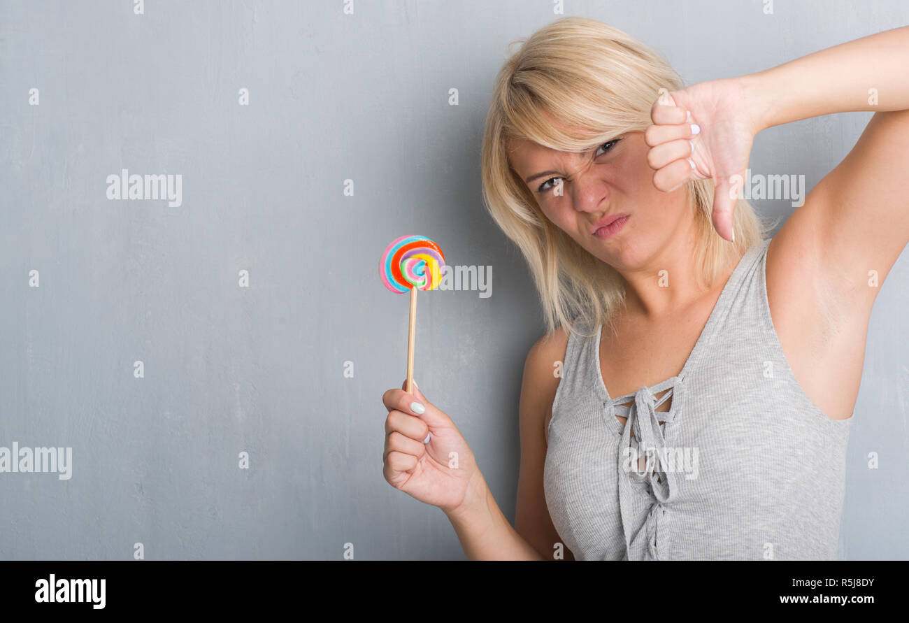 Caucasian adult woman over grey grunge wall eating candy lollipop with ...