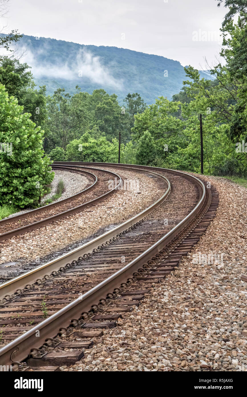 Double railroad tracks curve around a bend and into a misty mountain landscape in the Laurel ...