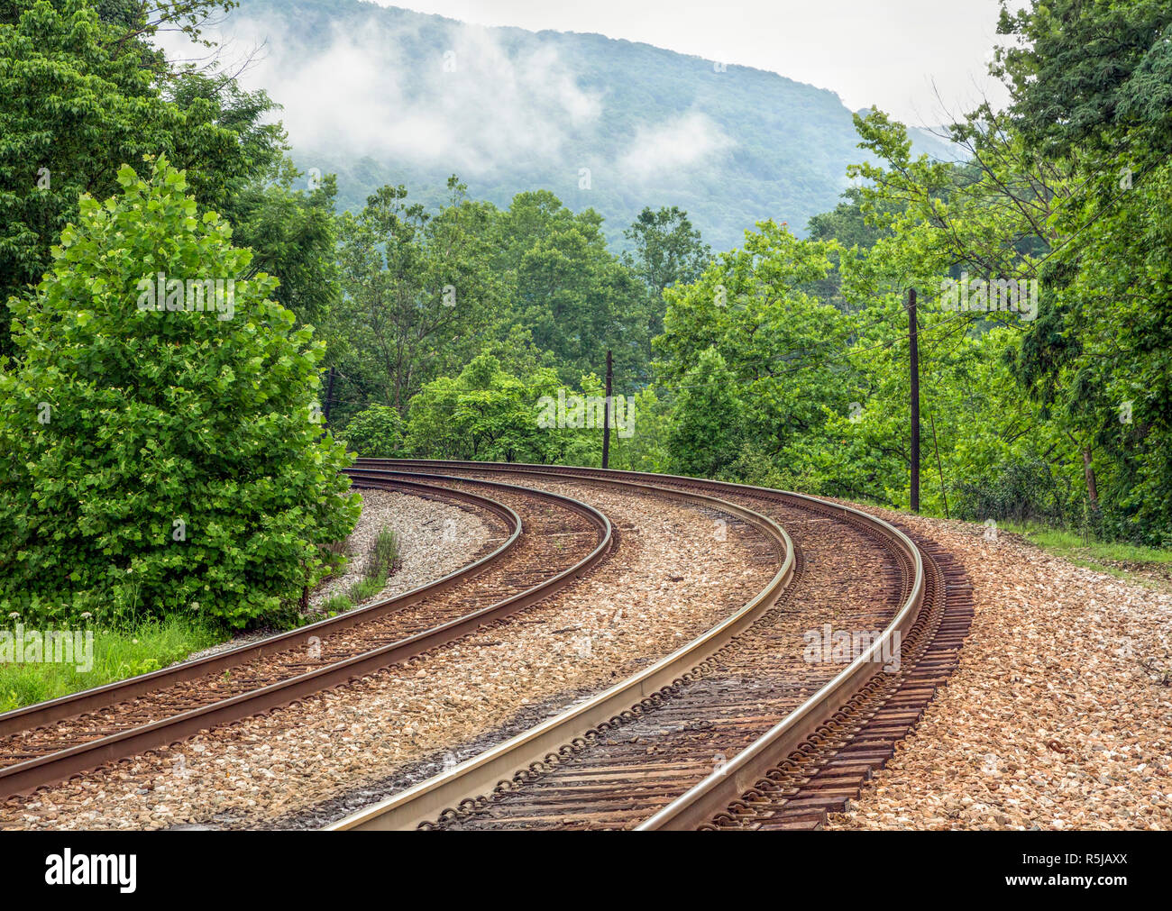 Double railroad tracks curve around a bend and into a misty mountain landscape in the Laurel ...