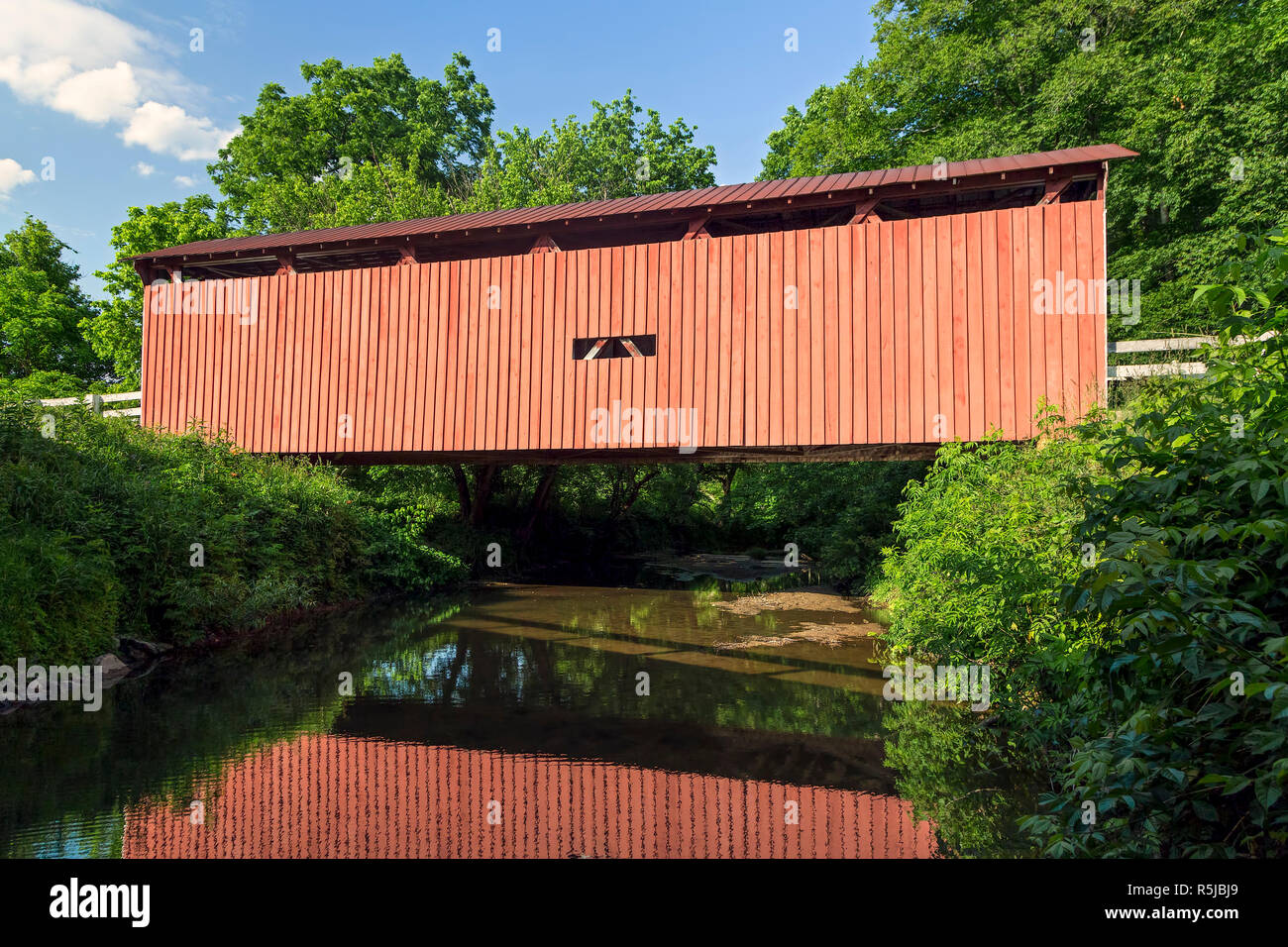 Built in 1878, the historic red Root Covered Bridge, is reflected in ...