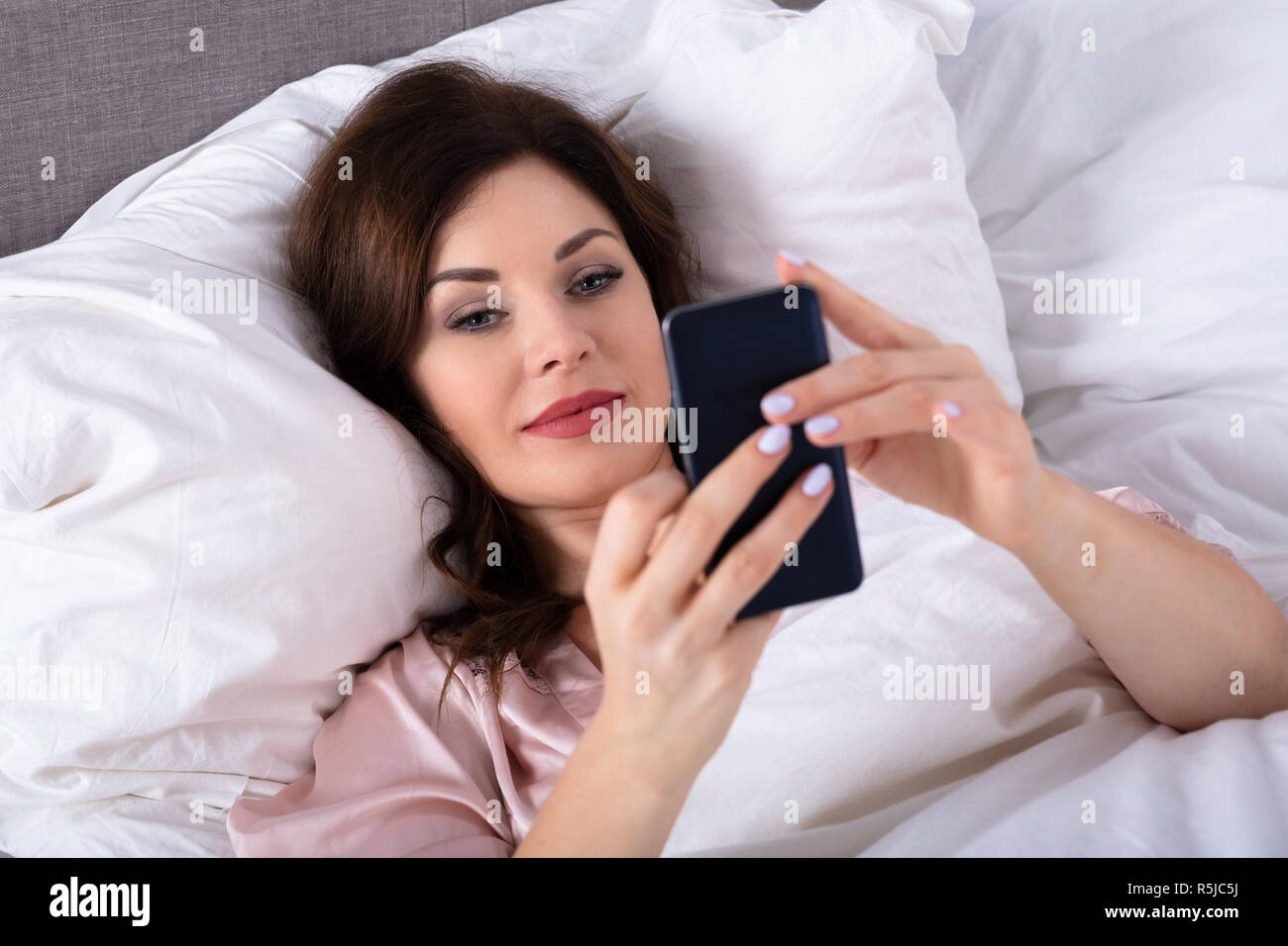 Beautiful Young Woman Lying On Bed Holding Mobile Phone Stock Photo - Alamy