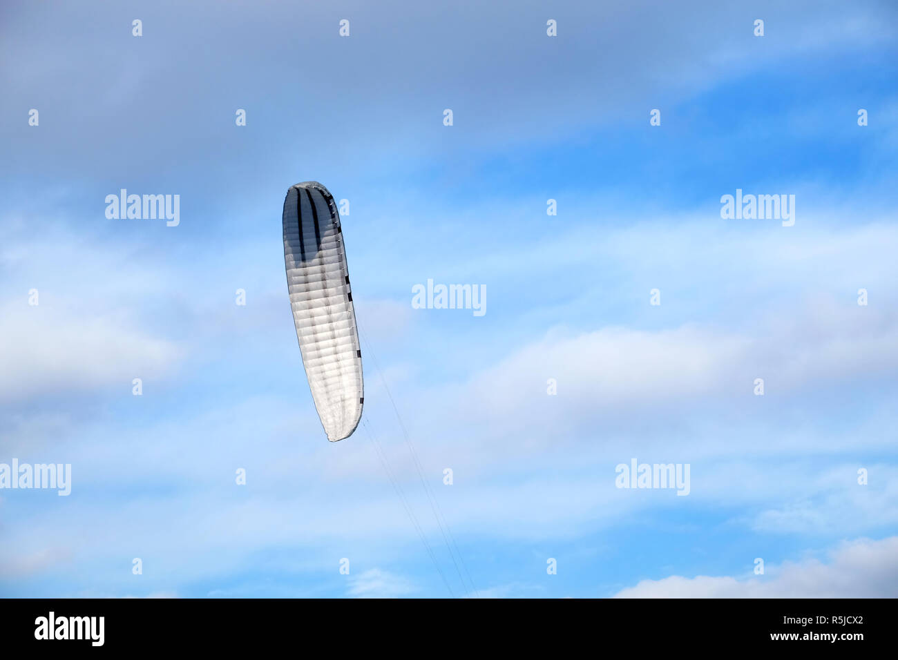 Big gray kite with long black stripes in bright blue sky with white ...