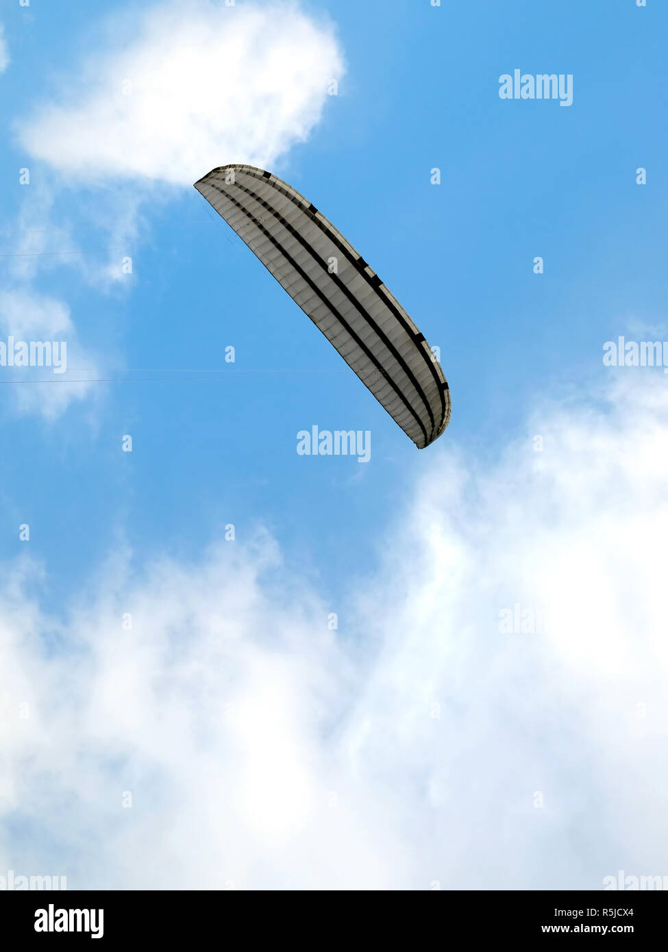 Big gray kite with long black stripes in bright blue sky with white ...