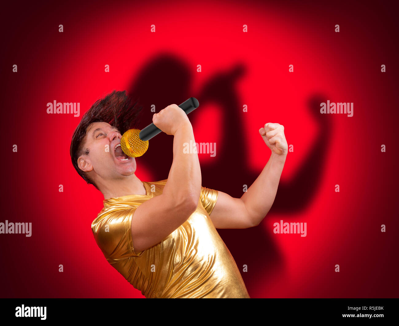The excited singer with a microphone with own shadow on red background ...