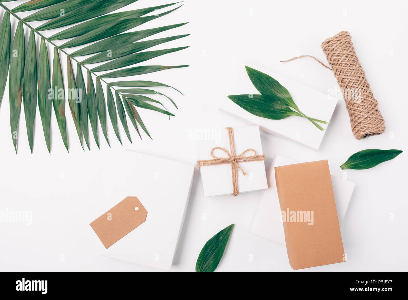 Stylish flat lay composition of palm leaf, gift boxes and twine, top view on white background ...